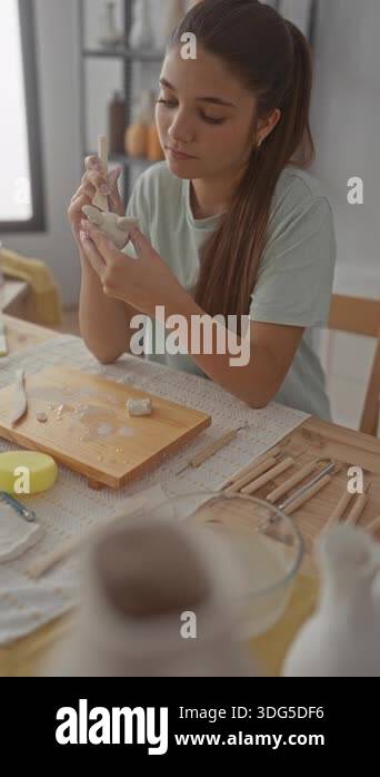 Teenage girl shapes smooth white clay vessel with carving tool and ...