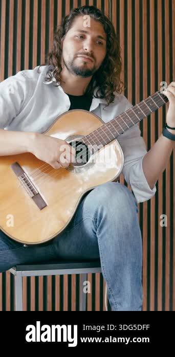 Long haired musician sitting on a stool and strumming an acoustic ...