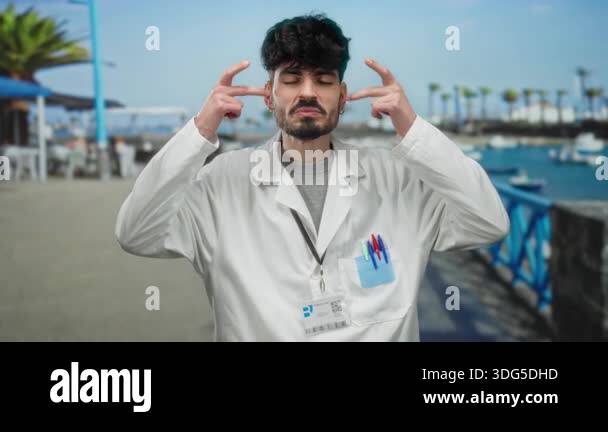Young man smiling at seaside port in lab coat under blue sky with boats ...