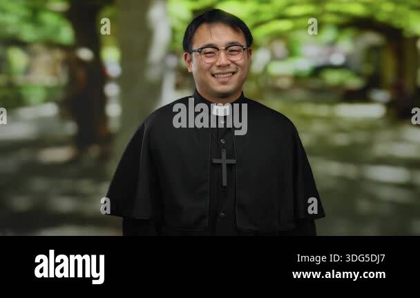 Asian priest in black robe smiling outdoors in sunny park with green ...