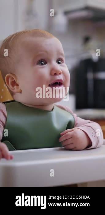 A happy infant girl laughs and opens her mouth wide while her mother ...