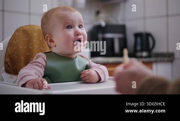 A happy infant girl laughs and opens her mouth wide while her mother ...