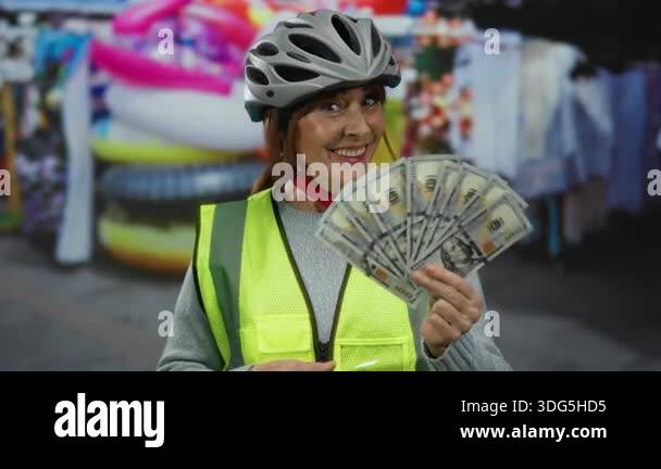 Hispanic senior woman with bike helmet and vest holds american dollars ...