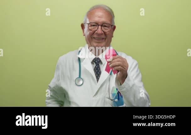 Senior male doctor in uniform smiling and holding a pink ribbon against ...