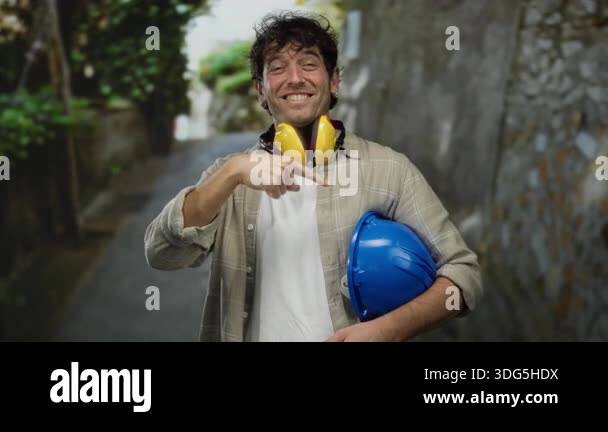 Smiling hispanic man pointing at a blue hardhat, wearing noise ...