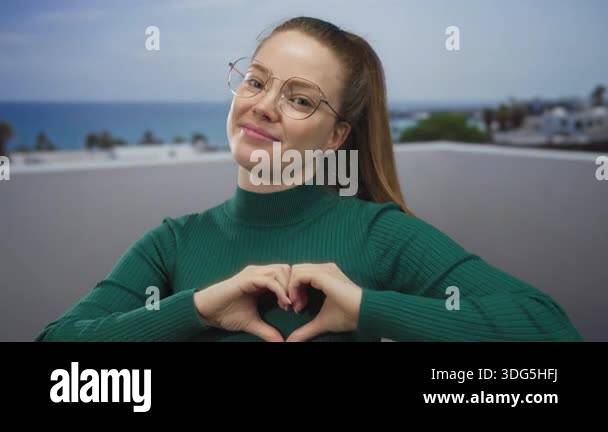Woman in green sweater shapes heart symbol with hands on building ...