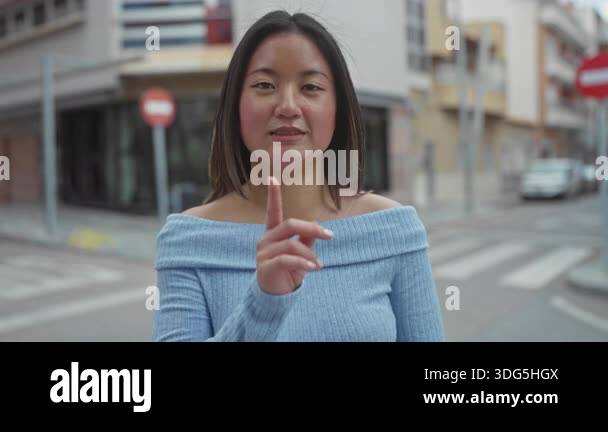 Woman in blue sweater gesturing shh while standing on street in city ...