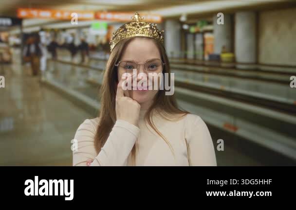 Woman wearing gold crown smiles and points finger to head while ...