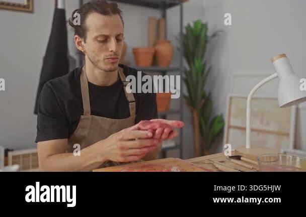 Man shaping red clay with stained hands on a wooden table in a pottery ...
