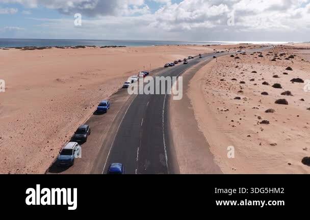 High aerial view shows a two lane road curving through ochre dunes by ...