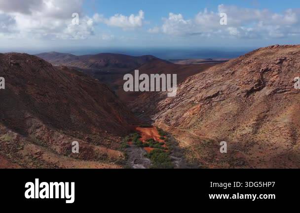 Aerial daylight glide and pan reveal rust ridges, layered rock, green ...