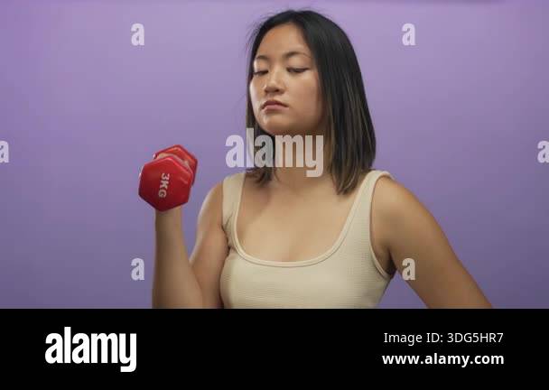 Young woman lifting dumbbell isolated against purple background looks ...
