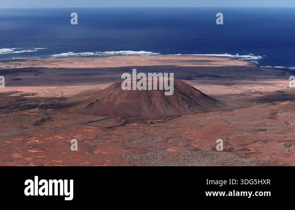 Aerial view shows a flattened volcanic cone, red brown lava plains ...