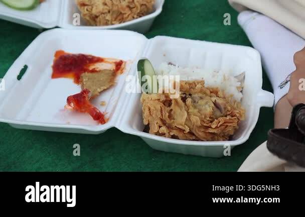 Hand picking crispy fried chicken from styrofoam container with rice ...