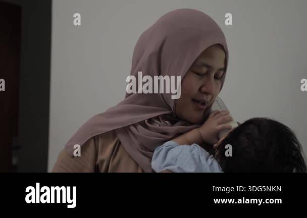 Asian muslim mother holding her baby while feeding her infant formula ...