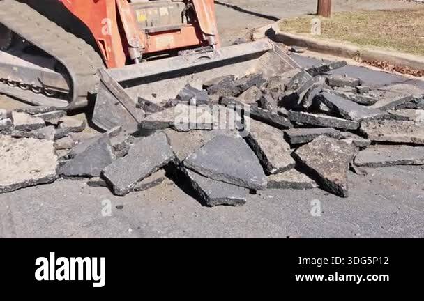 Construction worker uses skid steer loader to break up old asphalt in ...