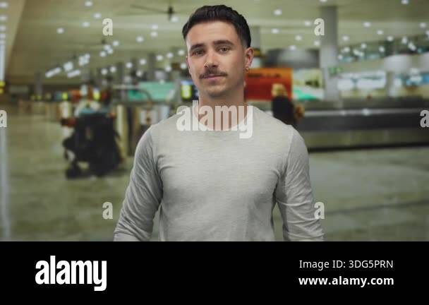 Young hispanic man wearing gray shirt embraces himself in busy indoor ...
