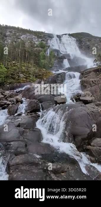 Vibrant white waterfall plunging from high rocky cliff into fast ...