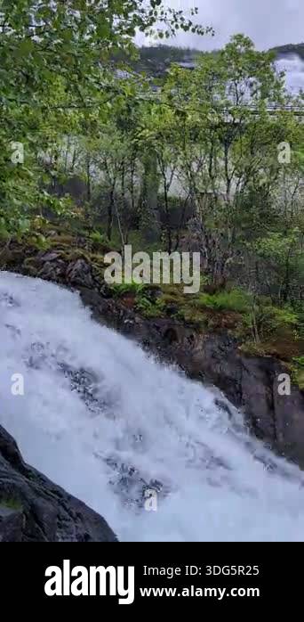 waterfall plunges from a high rocky cliff into a fast-flowing river ...