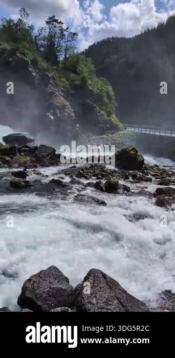 White water rushing over dark boulders in shallow mountain stream next ...