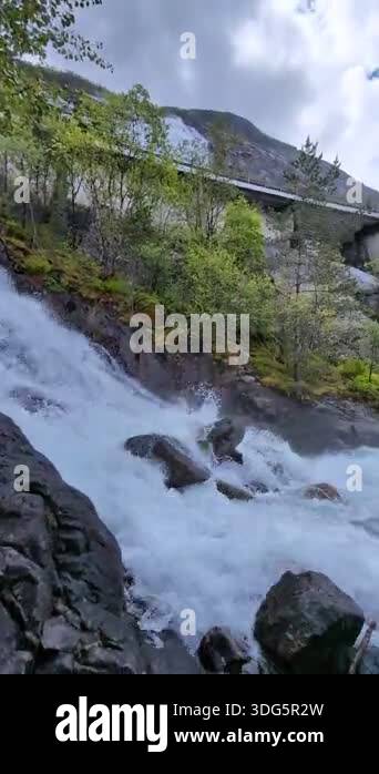 Vibrant white waterfall plunging from high rocky cliff into fast ...