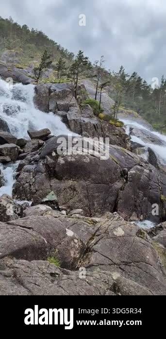 Vibrant white waterfall plunging from high rocky cliff into fast ...