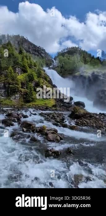 Large white waterfall plunging from high rocky cliff into fast flowing ...