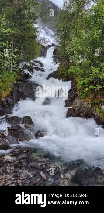 Vibrant white waterfall plunging from high rocky cliff into fast ...