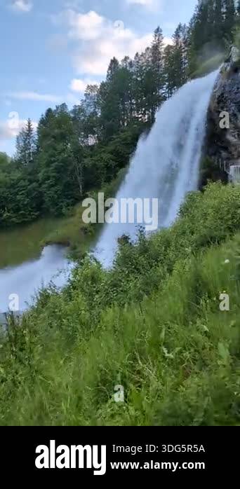 A large white waterfall plunges from a high rocky cliff into a pool ...