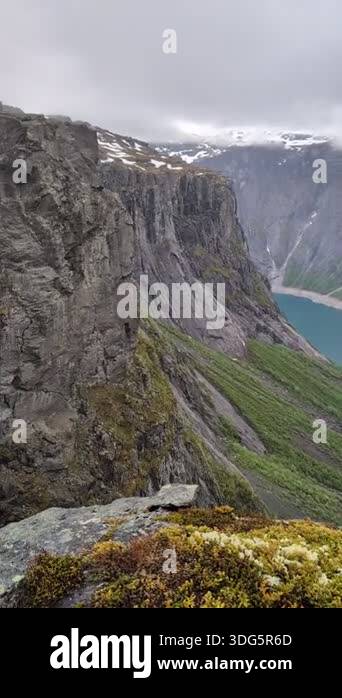 Vertical grey rock cliff towering over steep green mountain slope ...