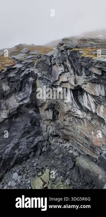 A close-up view reveals a rugged, vertical mountain wall made of dark ...