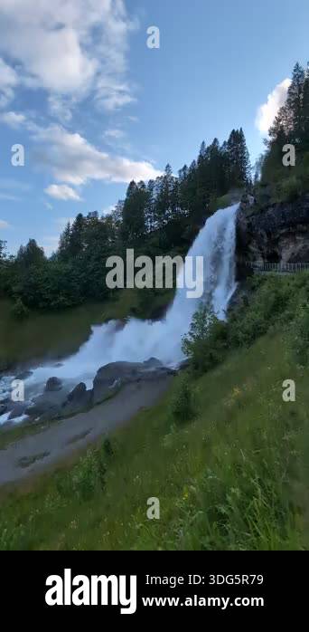 White waterfall plunging from high rocky cliff into pool framed by lush ...