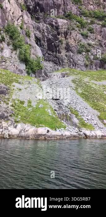 Steep, jagged cliff of dark, weathered rock, with lush green vegetation ...