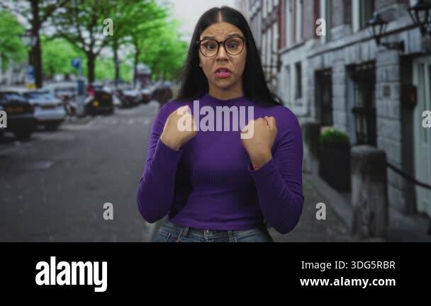 Woman wearing purple sweater pointing fingers to chest on street clad ...