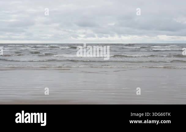 Sea waves roll onto a wide sandy beach under an overcast sky. Baltic ...