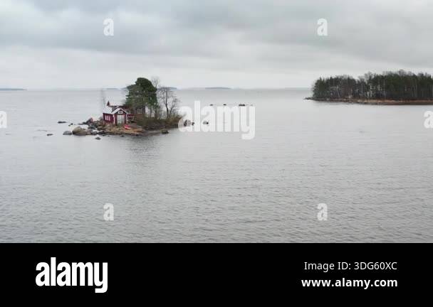 Red wooden cabin stands on tiny rocky skerry separated from mainland ...