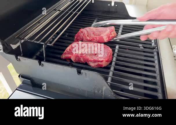Slow motion- Two raw ribeye steaks are placed onto a preheated outdoor ...