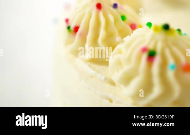 A macro shot captures piped frosting swirls on top of a white cake ...