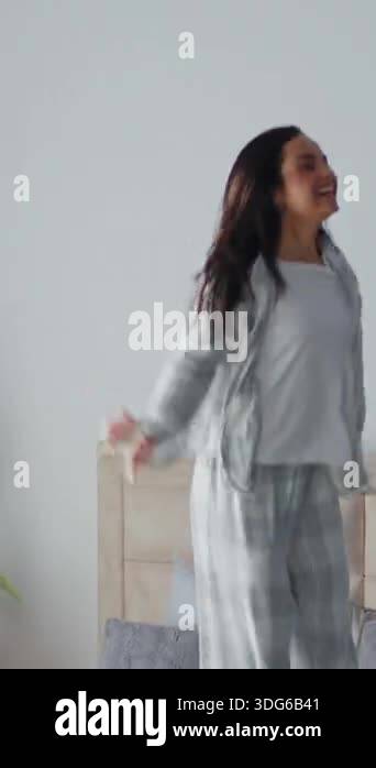 Happy excited Caucasian woman jumping on bed holding mobile phone ...