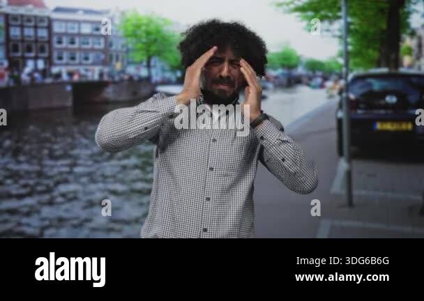 Man with curly hair raises both hands to block camera while standing by ...