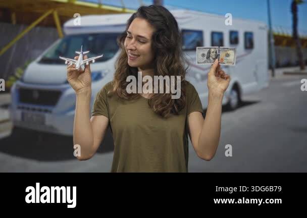 Woman smiling holds toy airplane and dollar bill in front of camper van ...