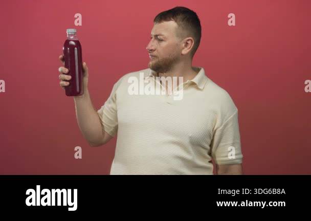 Man holding a tall bottle of purple juice and grimacing while ...