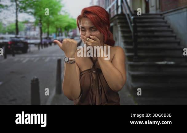 Woman covering mouth with hand and thumb pointing behind on a city ...
