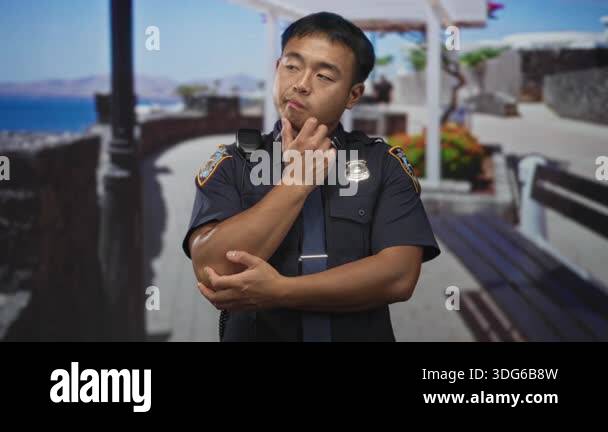 Man in police uniform standing outdoors on sunlit street touching chin ...