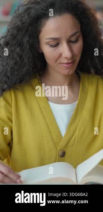 Hispanic Arab Indian woman reading book library looking at camera ...