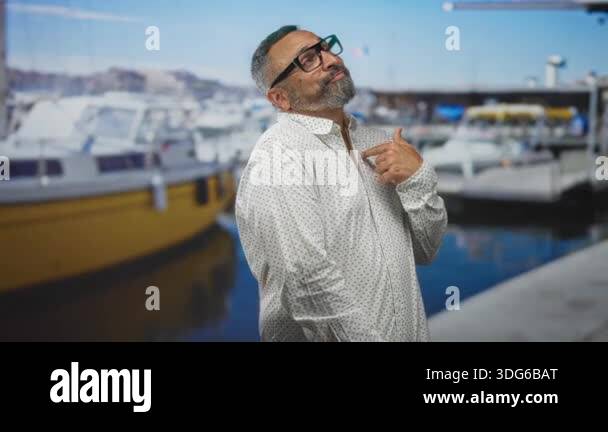 Man points thumb to chest beside moored boats on street near a marina ...