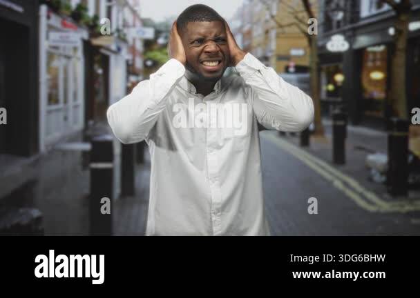 Man covers ears with hands on a narrow street, grimacing and squeezing ...