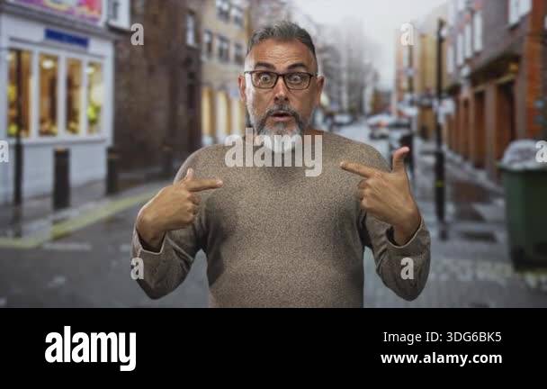 Man points thumbs to chest on a city street wearing glasses and brown ...