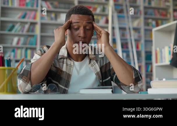 African American man male student in library massaging temples stressed ...