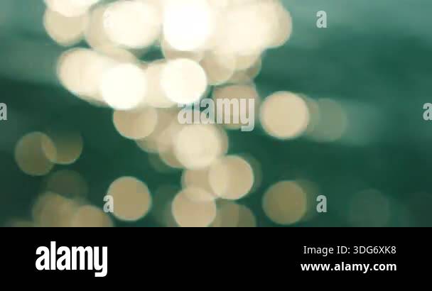 Glowing white bokeh highlights float on emerald sea water in motion ...